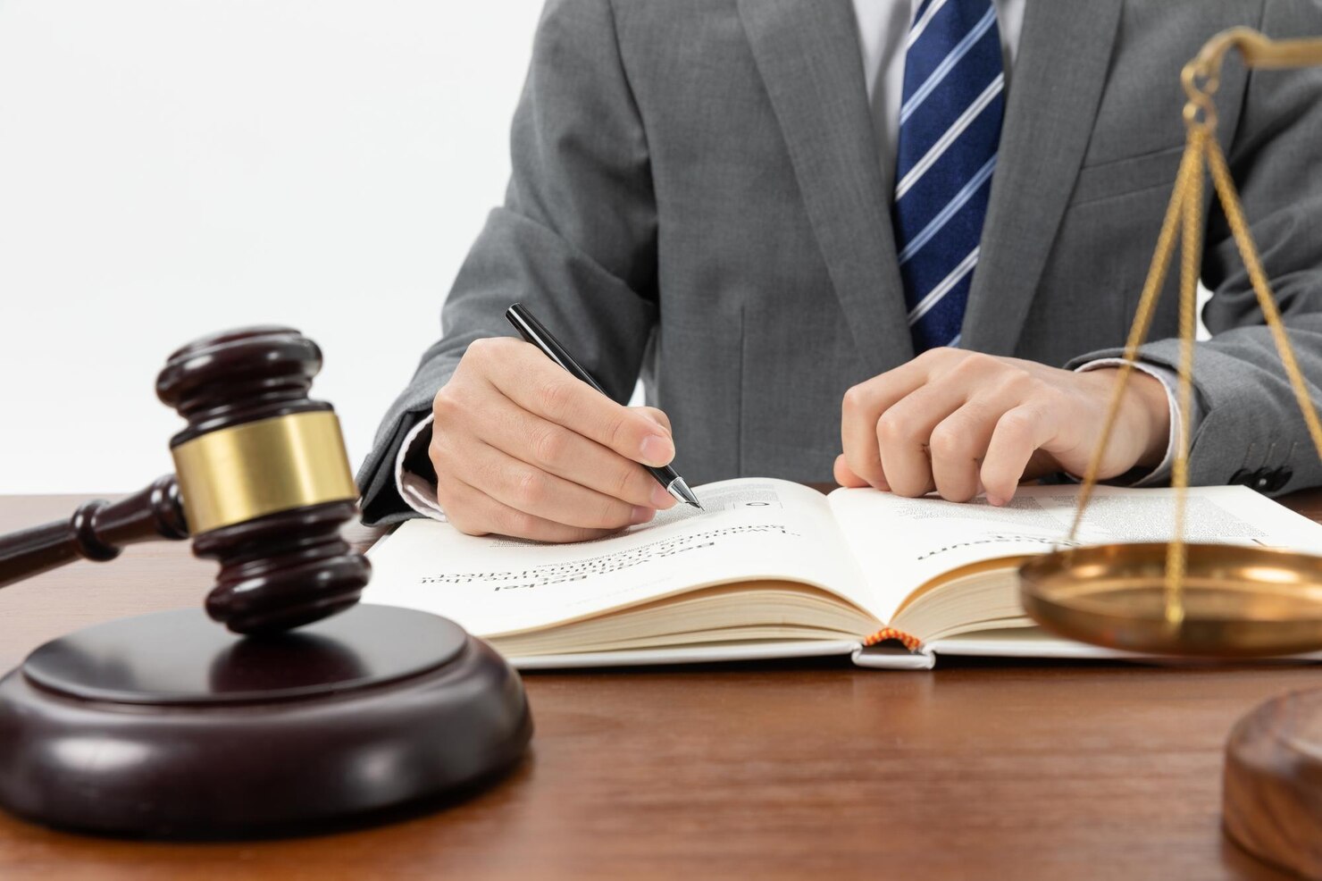 Person writing on book with gavel and balance on the table